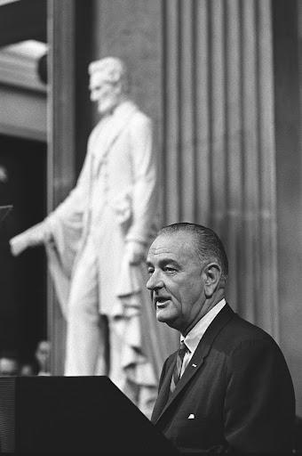 Pres. Lyndon B. Johnson delivering remarks from behind a podium. Statue ...
